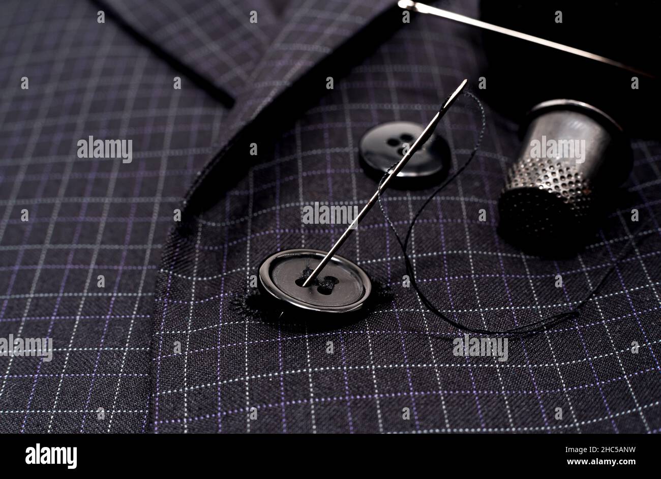 A needle and thread sews up a button on a plaid suit. Thimble. Textile ...