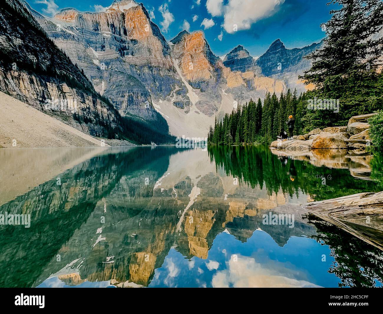 Reflective calm lake surrounded by rocky mountains and pine trees in ...