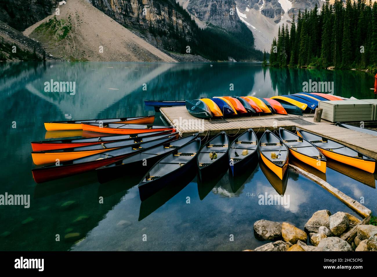 Calm lake with a pier and colorful boats surrounded by mountains and ...