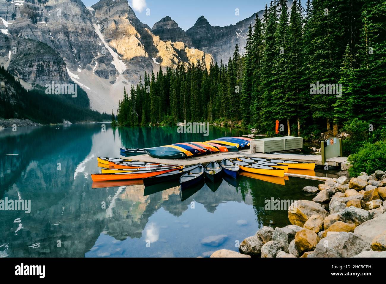 Calm lake with a pier and colorful boats surrounded by mountains and ...