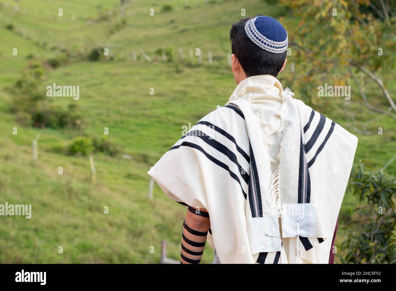 Jewish man praying with talit, kippah and tefillin in nature with ...