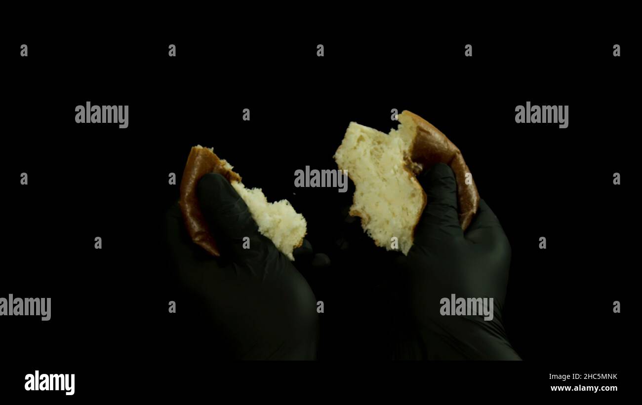 Close up of baker man hands tear hot bread isolated on black background ...