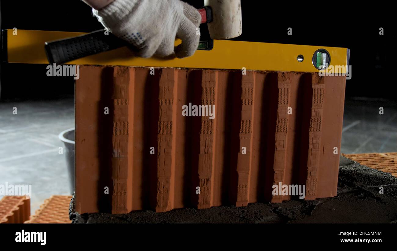 Industrial background, worker in gloves using hammer for laying brick ...