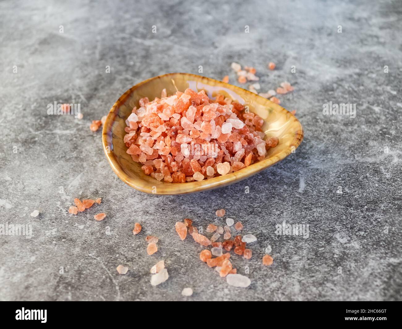 Pink Himalayan coarse rock salt on a little brown plate on gray ...