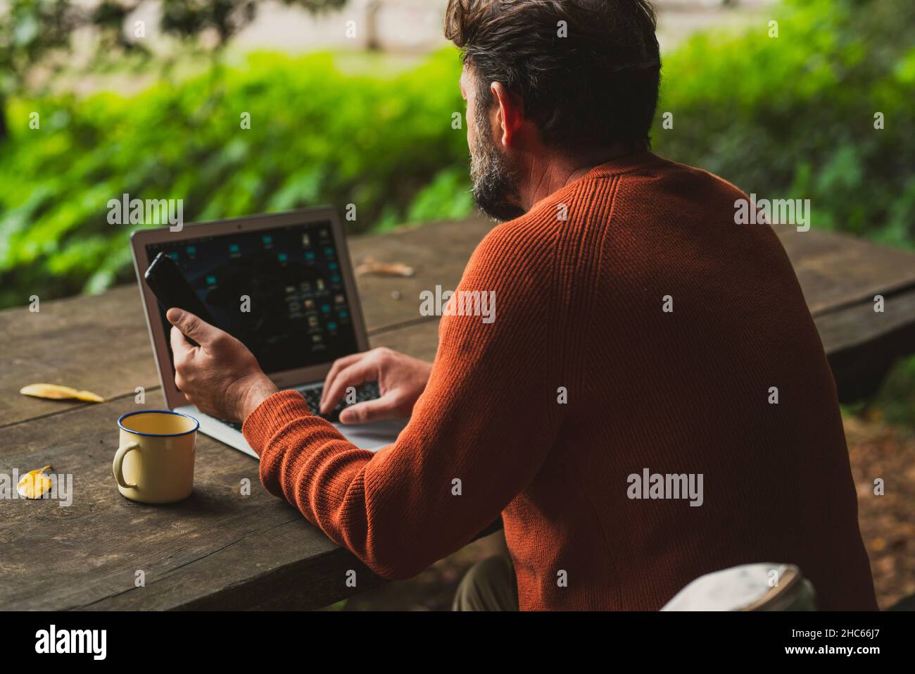 Back view of a man working with mobile phone and laptop computer in ...