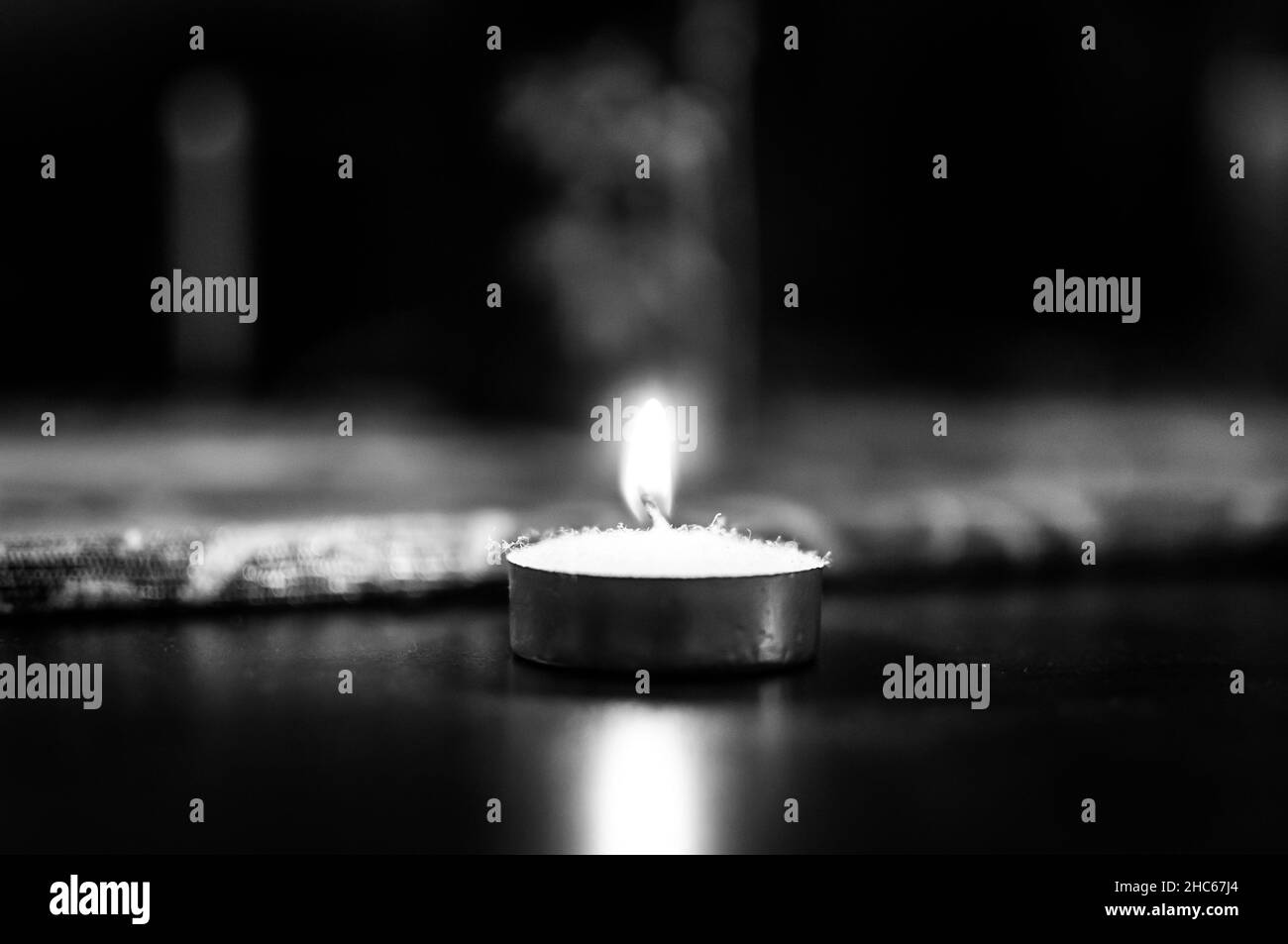 Closeup greyscale of small candle lightening on a surface with a blurry ...