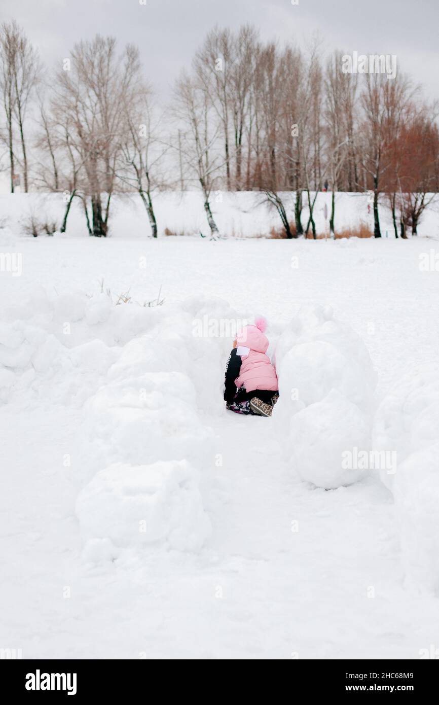 kid crawling in snowdrift in winter in park wearing warm winter clothes ...