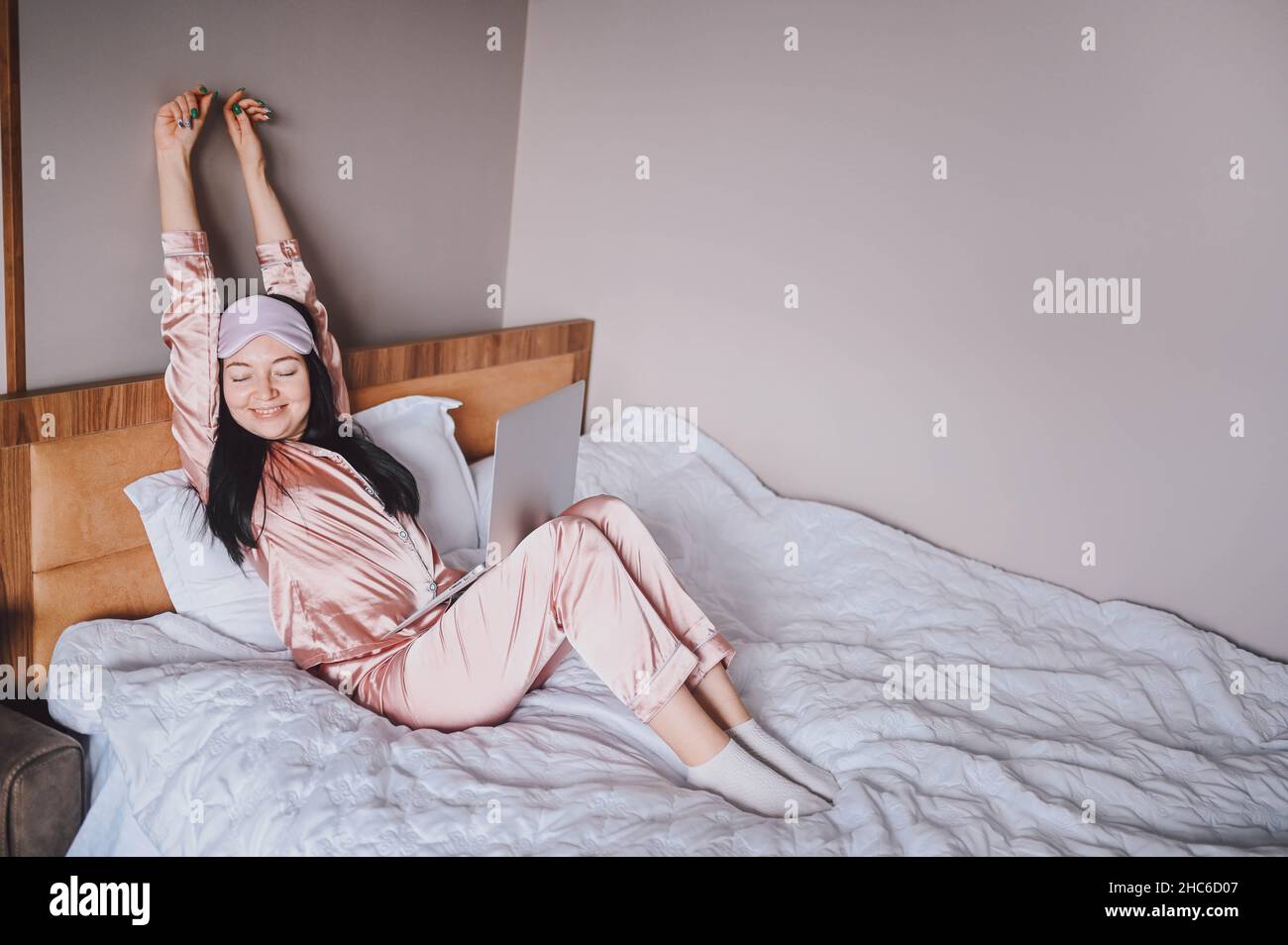 Attractive smiling young woman in pink silk pajamas and eye sleeping ...