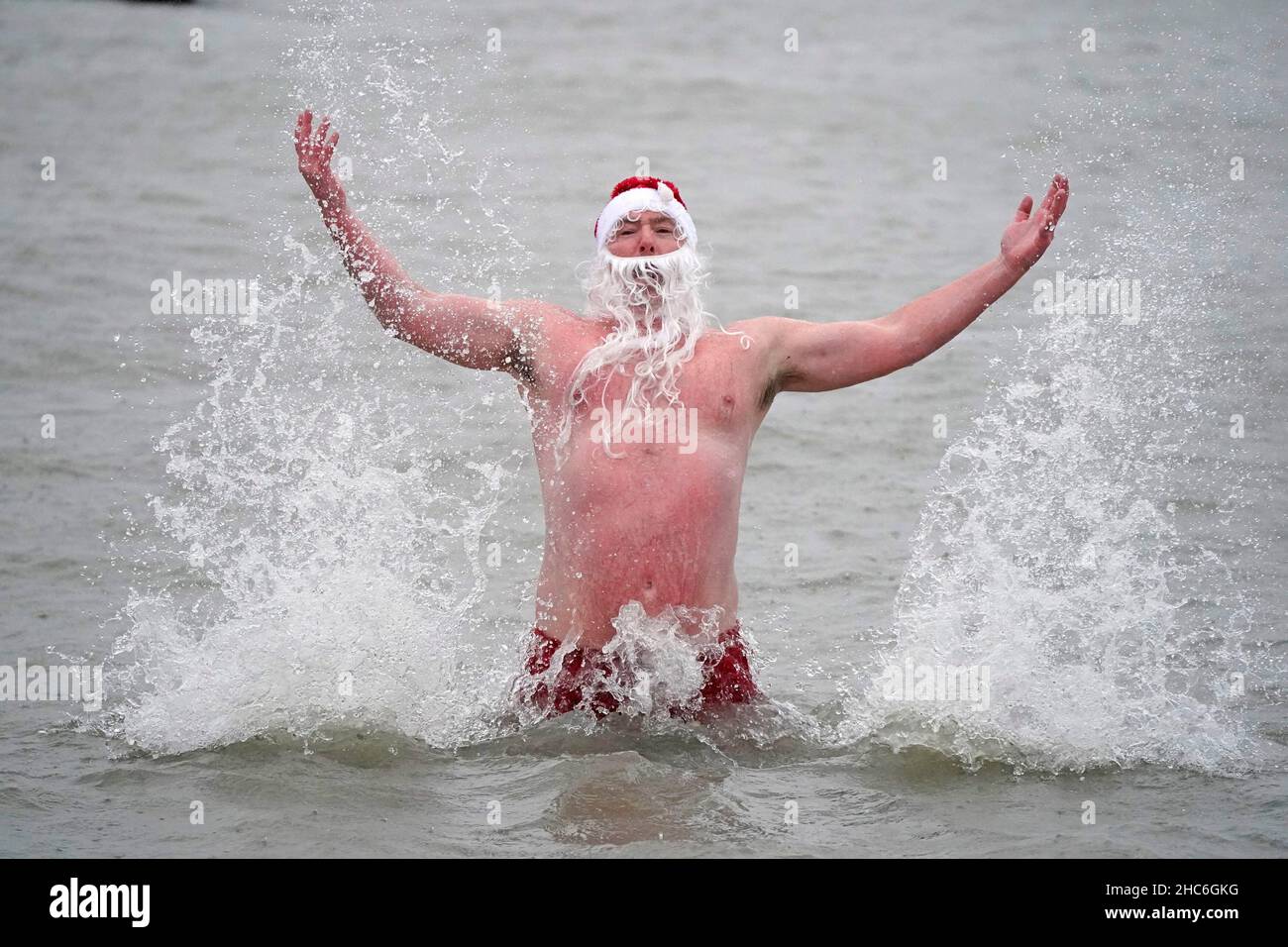 Patrick Corkery wears a santa hat and beard as waves crash over him ...