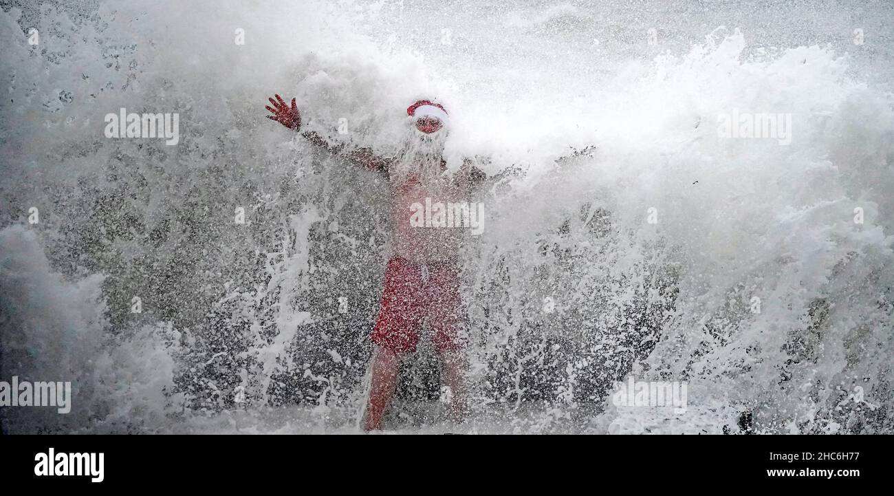 Patrick Corkery wears a santa hat and beard as waves crash over him ...