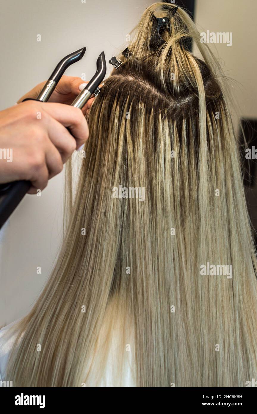 Hair extension process of a young woman in a beauty salon close-up ...