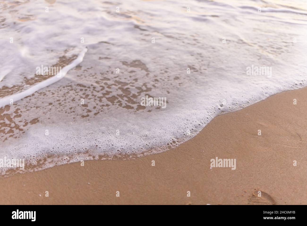 Sunny day at the beach with shallow, foamy sea tides washing over the ...