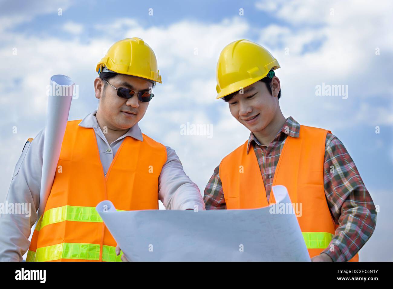 Two Asian engineers or technicians wear a yellow helmet with an orange ...