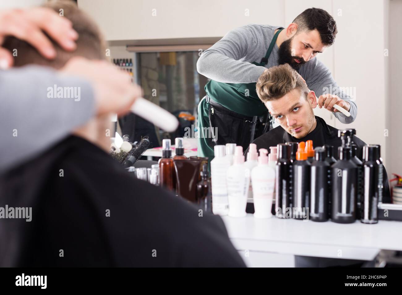 attentive guy stylist creating haircut for man client at hairdressing ...