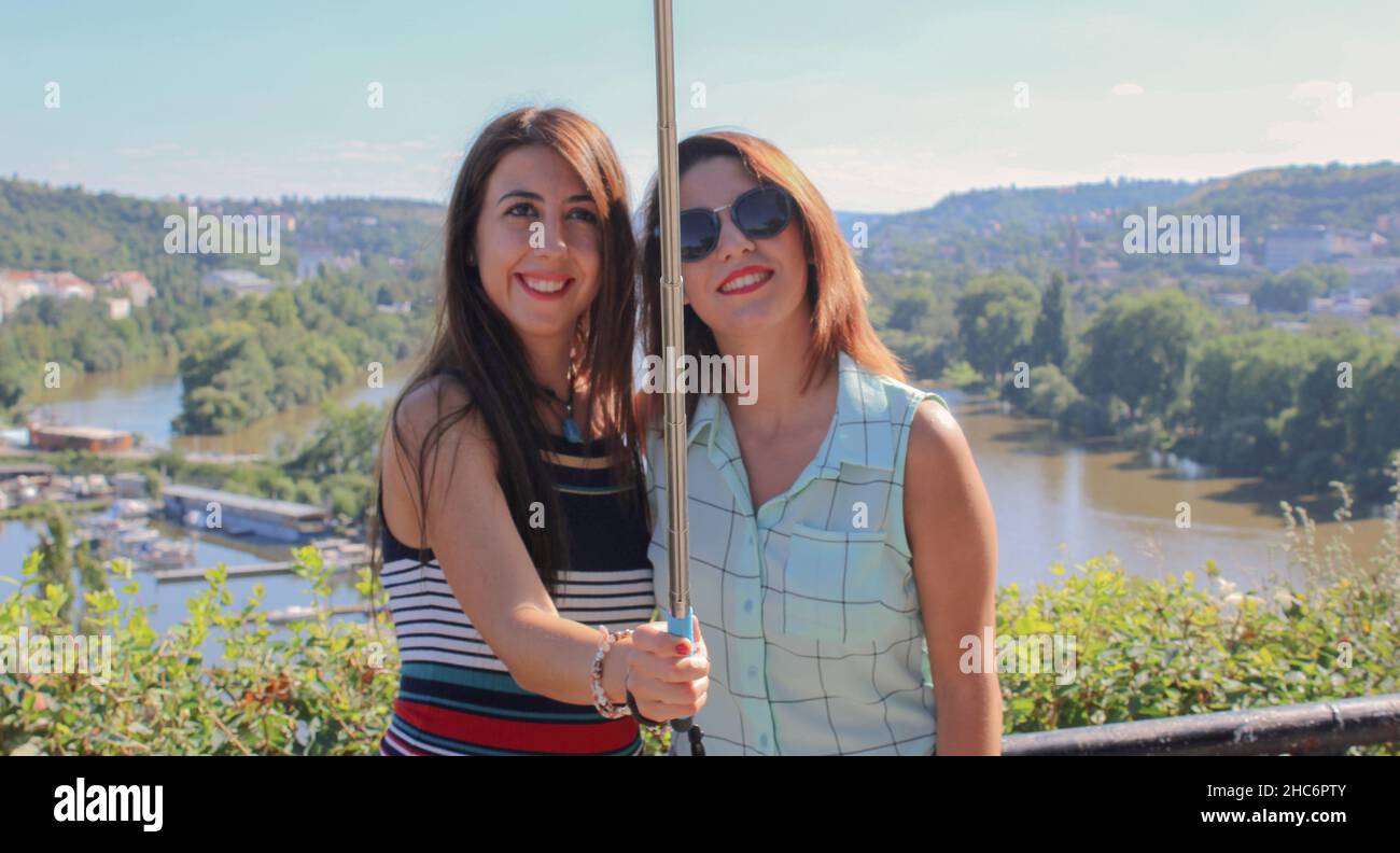 Two friends together happily taking selfie with selfie stick outdoors in tourist park in Prague ...