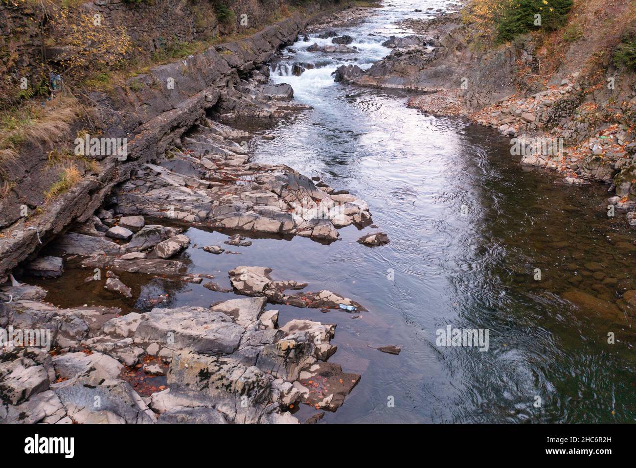 Narrow river stream running past mountain foot with green coniferous ...