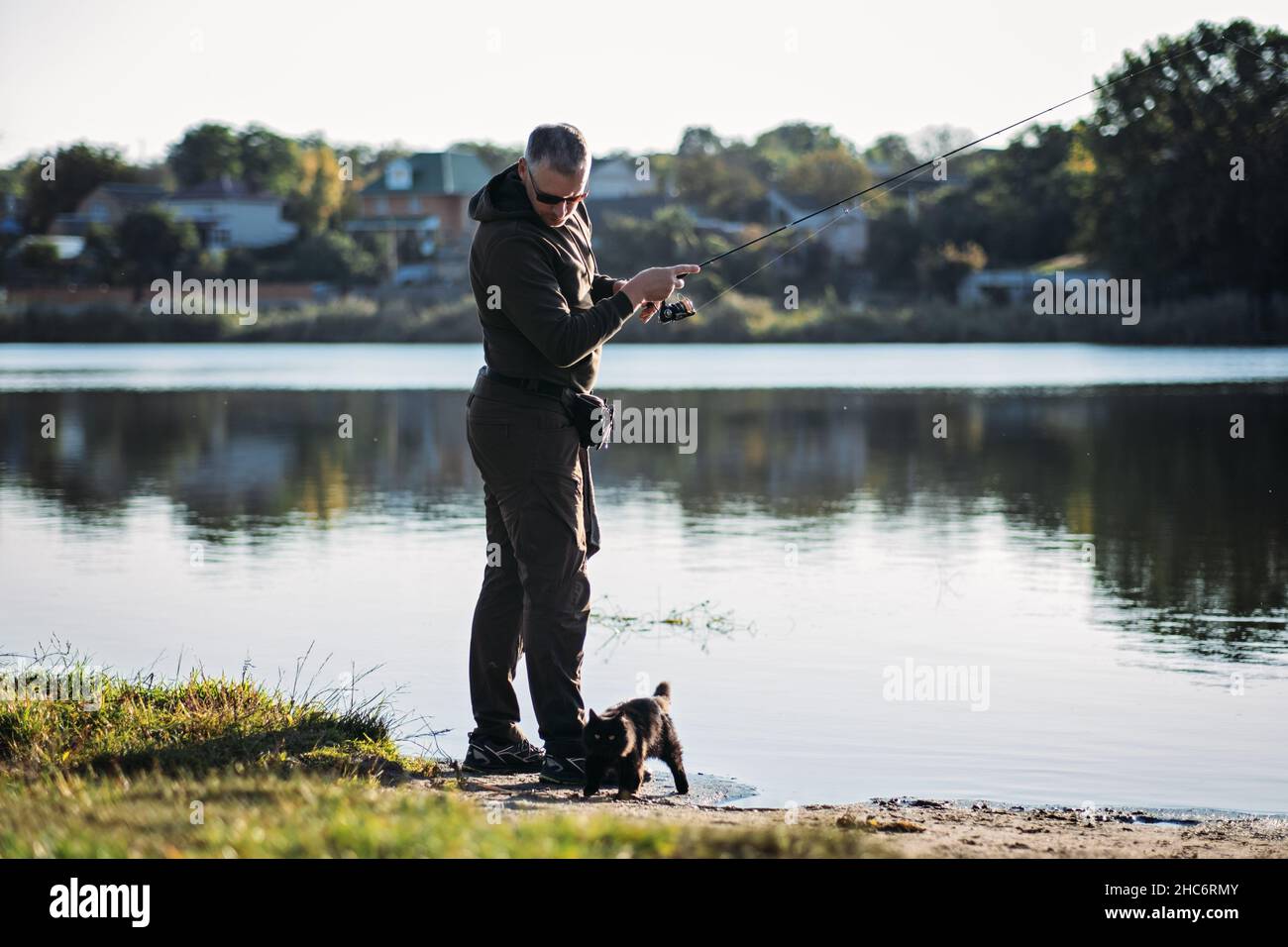 Fisherman with spinning rod and cat near him on nature background ...