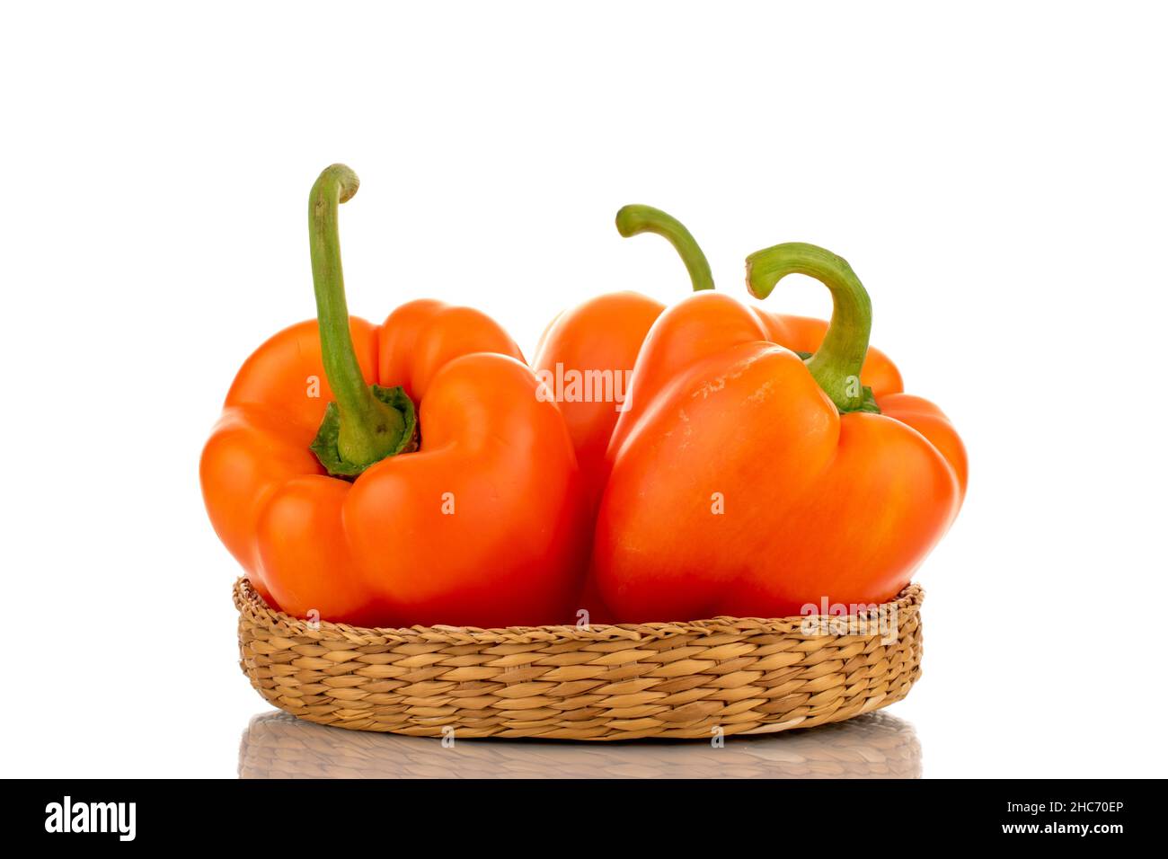 Three ripe orange sweet peppers on a straw plate, close-up, isolated on ...