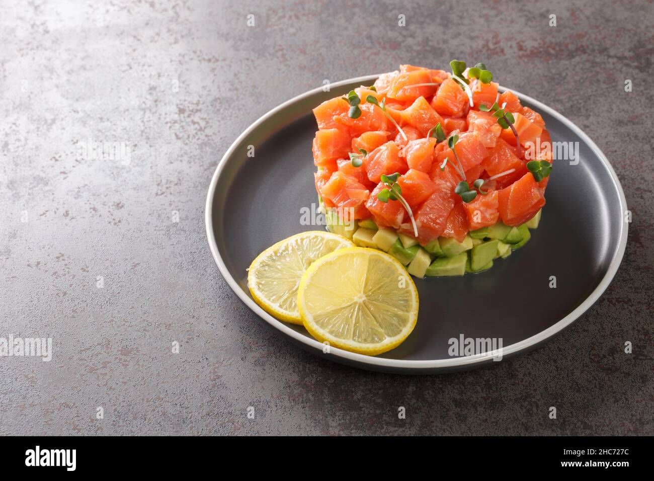 Salmon tartare with slices of avocado, served with lemon and microgreen ...