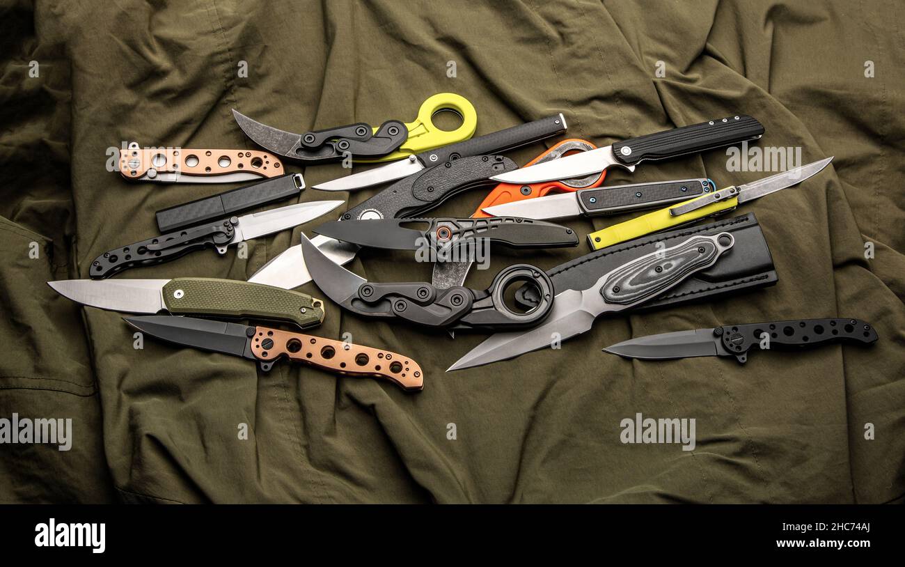 A variety of folding and pocket knives lie on khaki fabric. A versatile ...