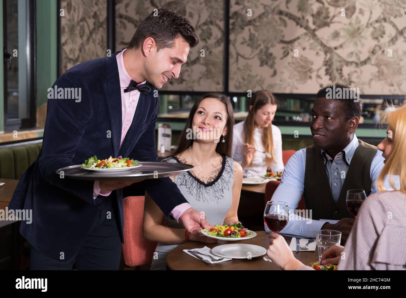 Smiling waiter serving visitors of restaurant Stock Photo - Alamy