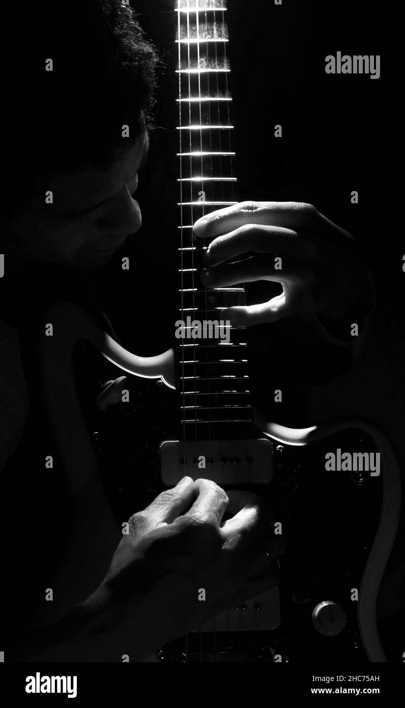 Vertical closeup of a man playing on an electric guitar under sun rays ...