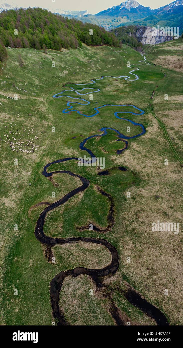 Aerial, vertical shot of a landscape with a bendy river, lawns, and ...