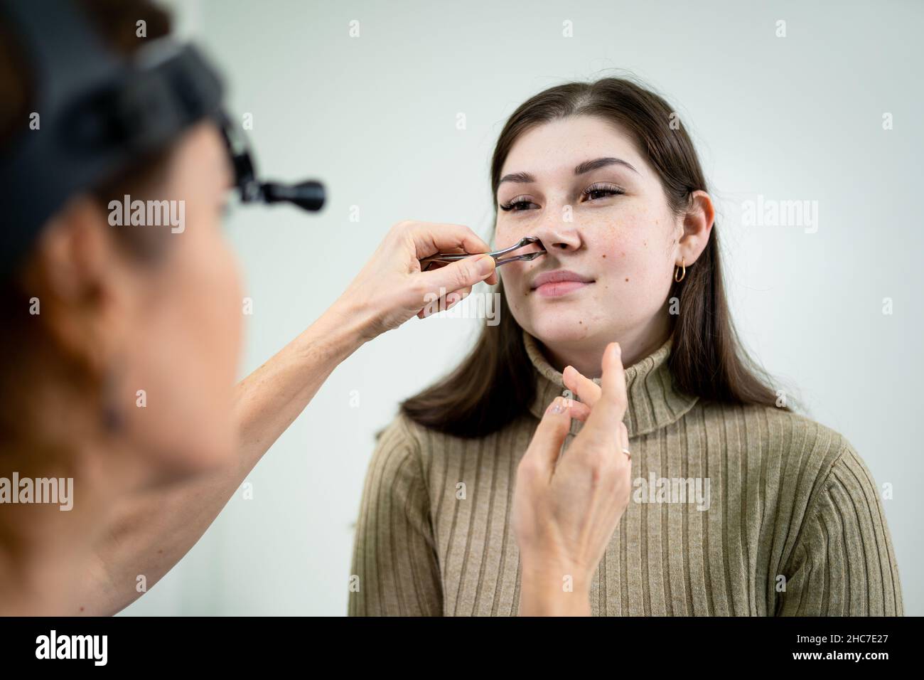 Professional female doctor otorhinolaryngologist doing nose examination ...