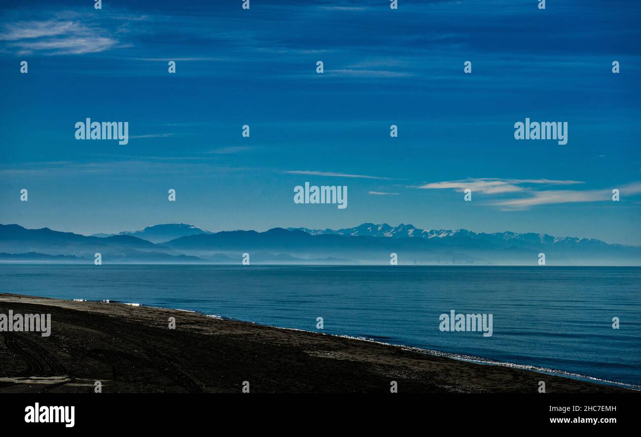 Black volcanic sand beach and Caucasus mountains with snow peaks in ...