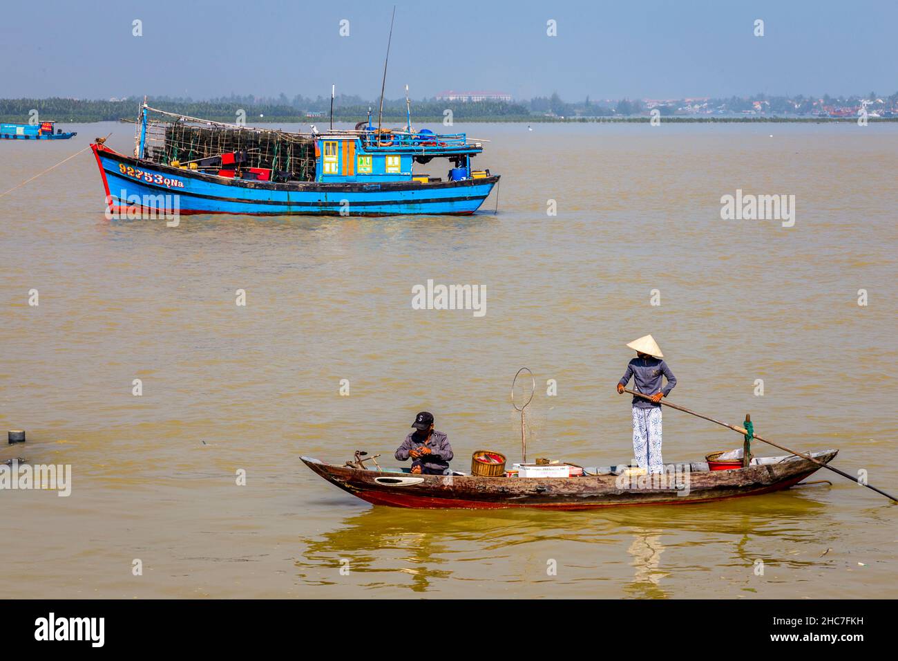 Girl with long oar moving her small boat in front of a trowler in a Hoi ...