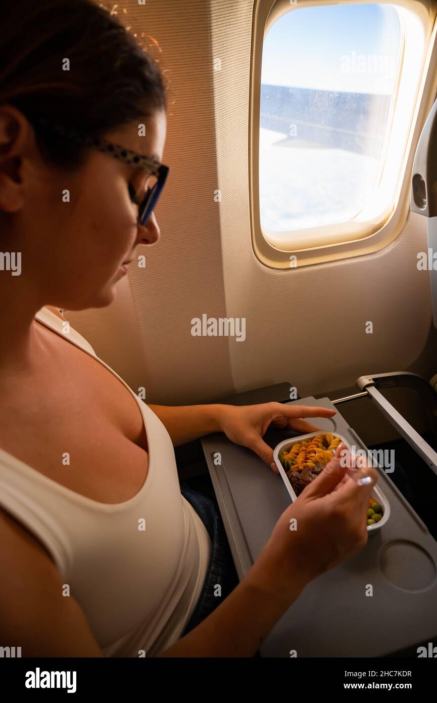 Caucasian woman flying in economy class and eating lunch from a tray ...
