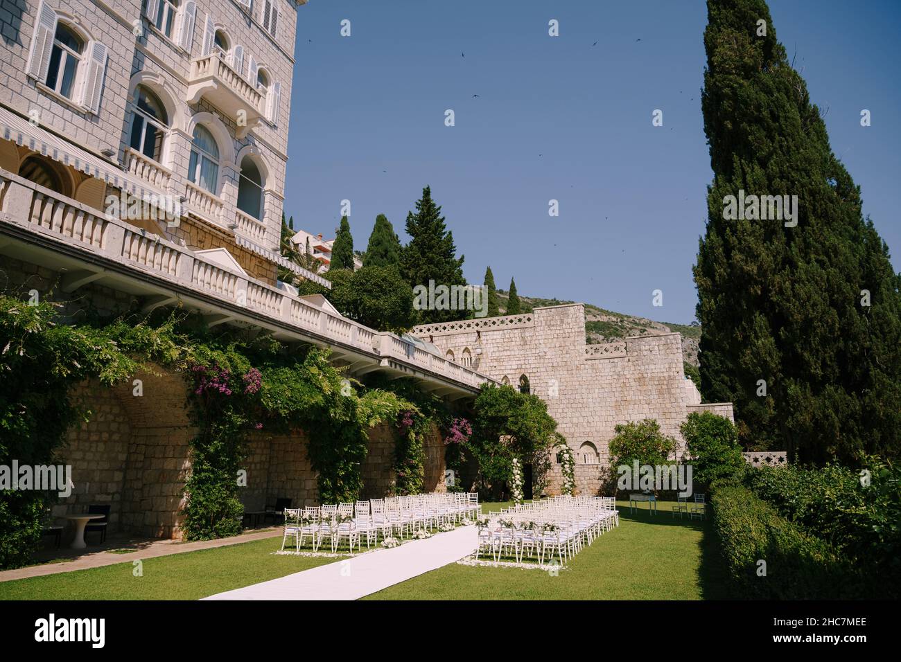 White path lies between rows of chairs in the garden near a beautiful building with balconies ...