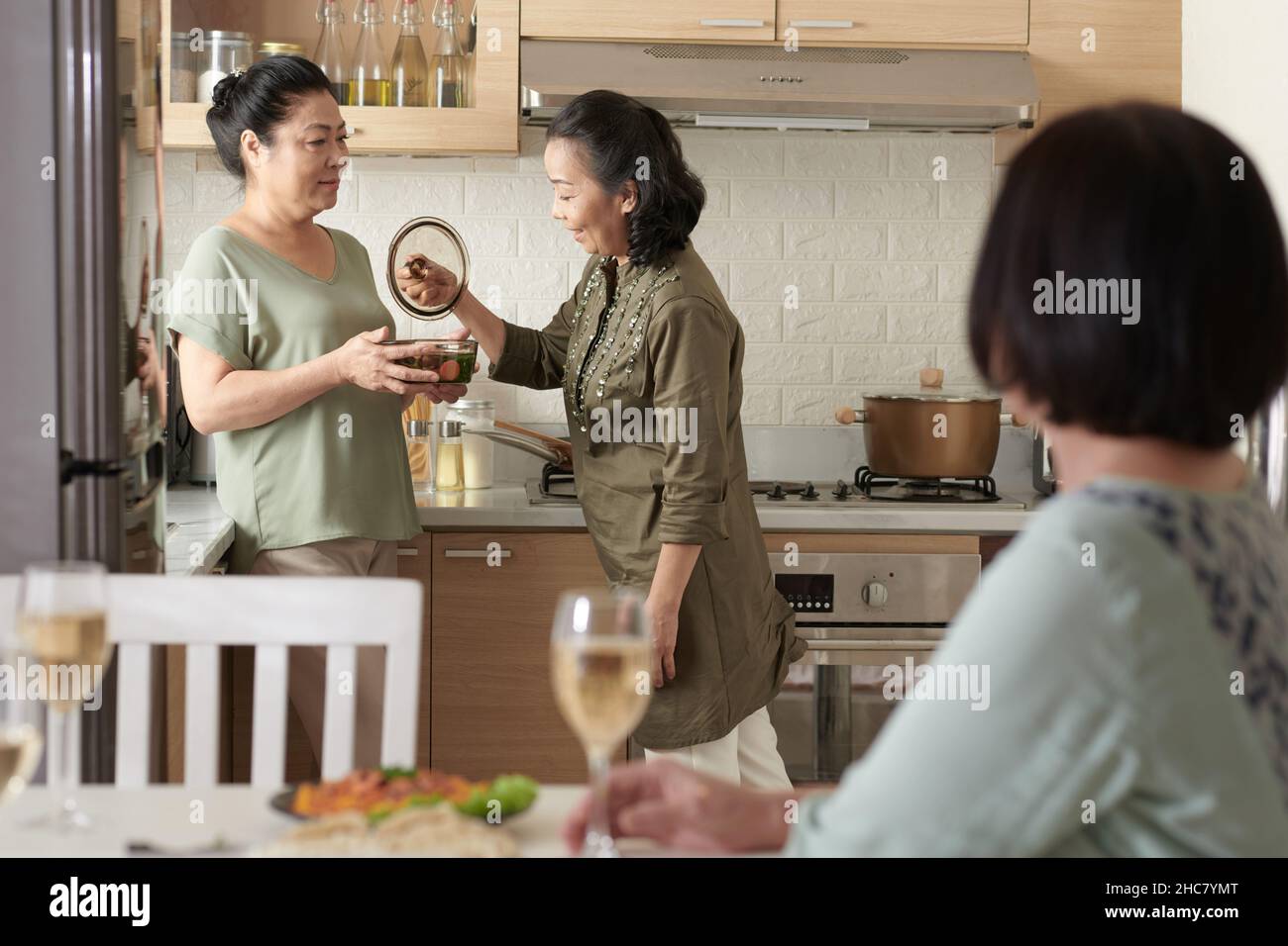 Senior woman helping friend with cooking and serving dinner Stock Photo ...