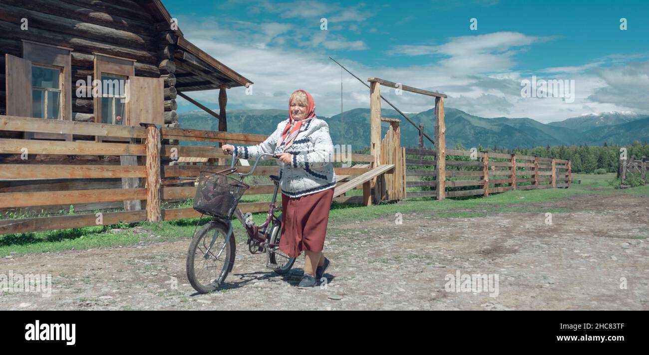 22nd of June, Russia, Altay, mature woman with bike on the street on ...