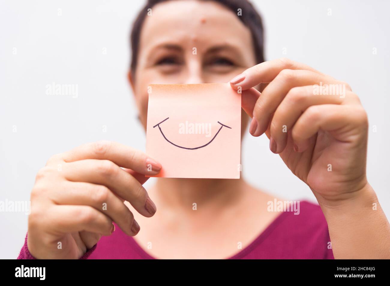 Woman hiding behind sheet of paper with happy face against wall Stock ...