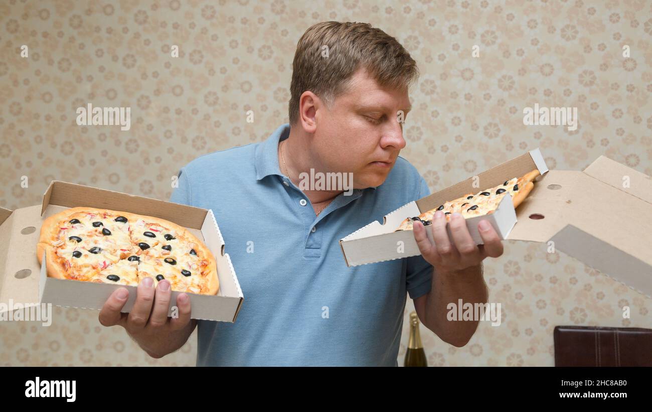 A glutton man with two pizzas in the kitchen inhales the aroma with ...