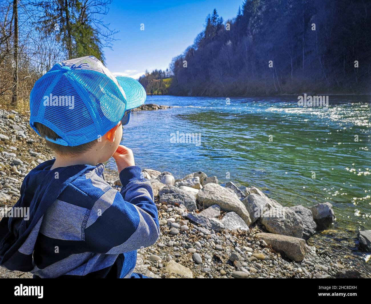 little boy stands on the bank of river, magnificent forest and its ...