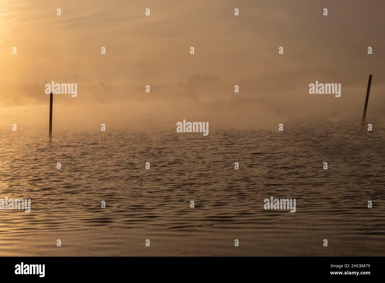 A cold sunrise in the winter over a lake with veils of mist creating a ...