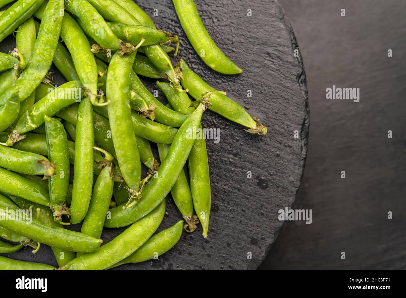 Fresh green peas on black plate. Bright green pea pods. Top view ...