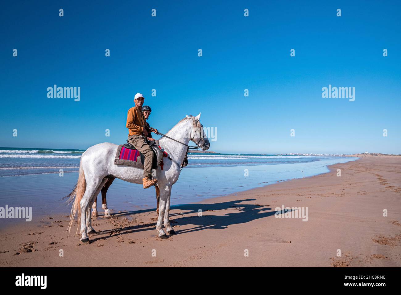 Man and woman riding horses along shoreline at beach against clear sky ...