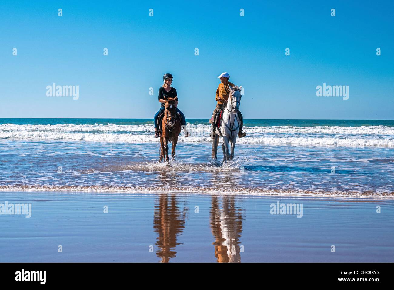 Man and woman riding horses along shoreline at beach against clear sky ...
