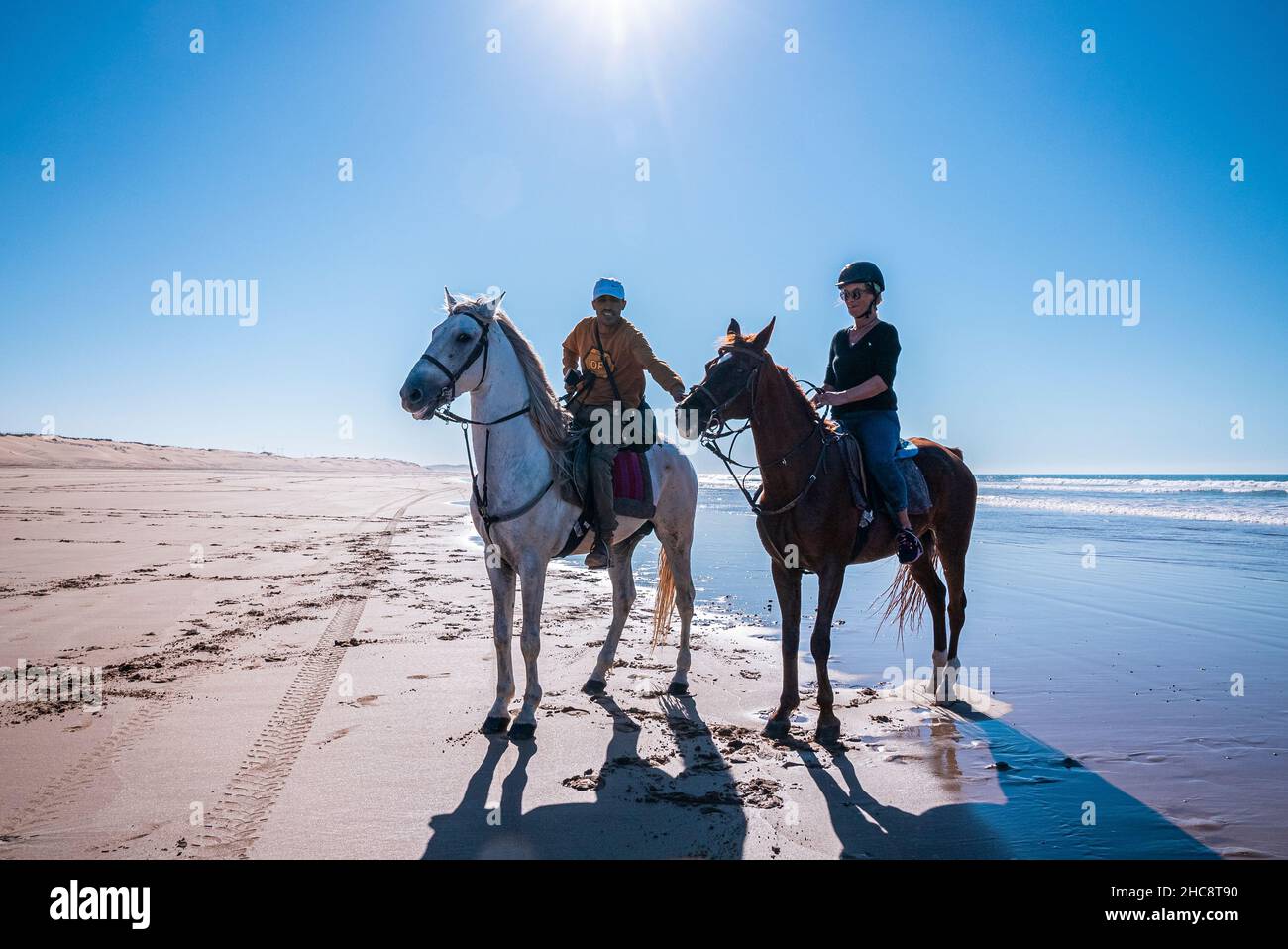 Man and woman riding horses along shoreline at beach against clear sky ...