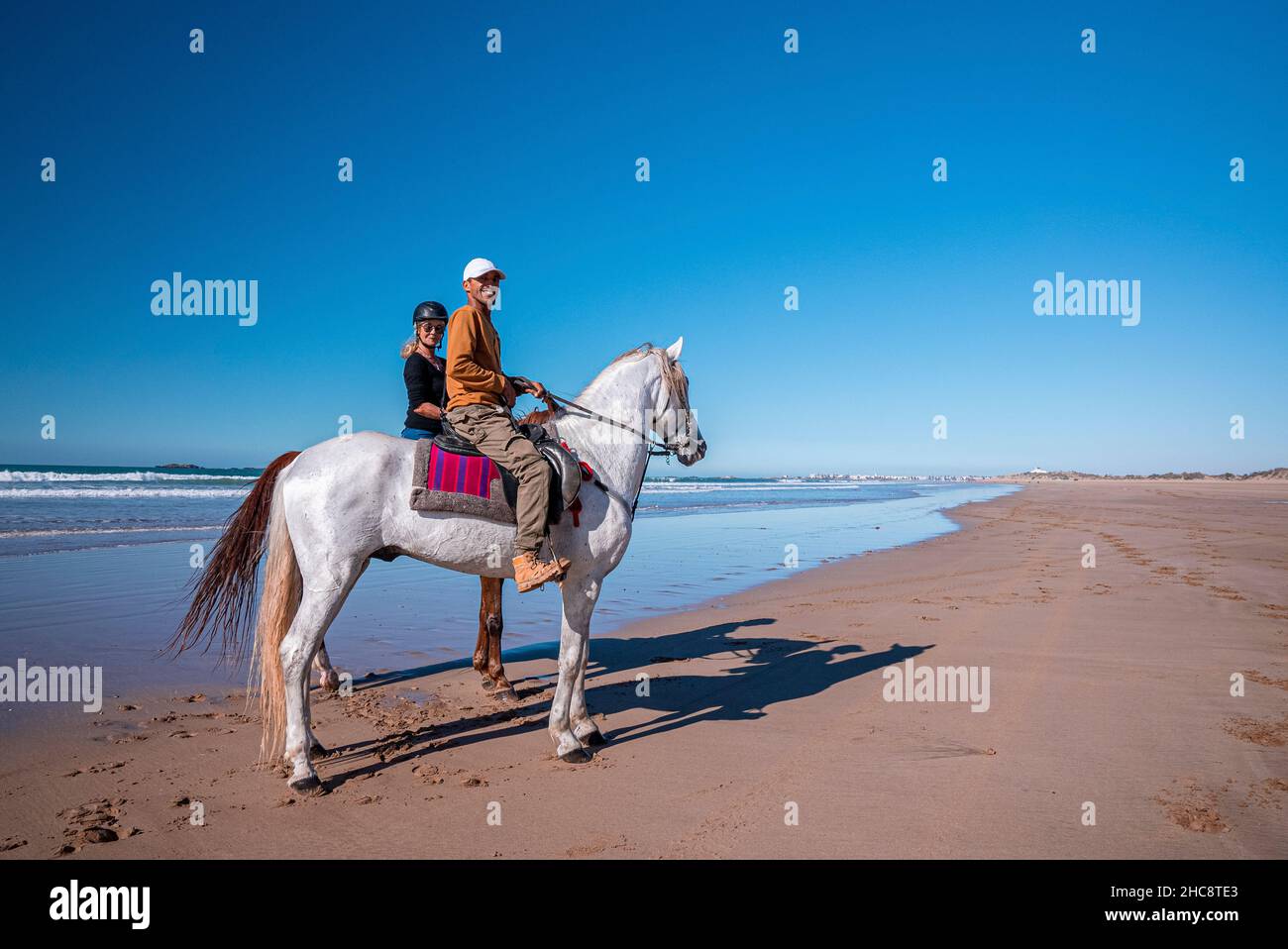Man and woman riding horses along shoreline at beach against clear sky ...