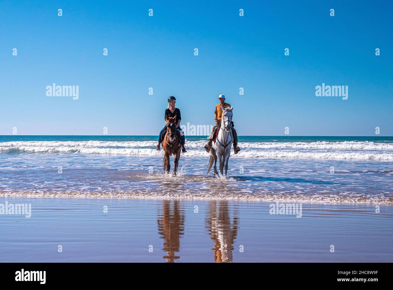 Man and woman riding horses along shoreline at beach against clear sky ...