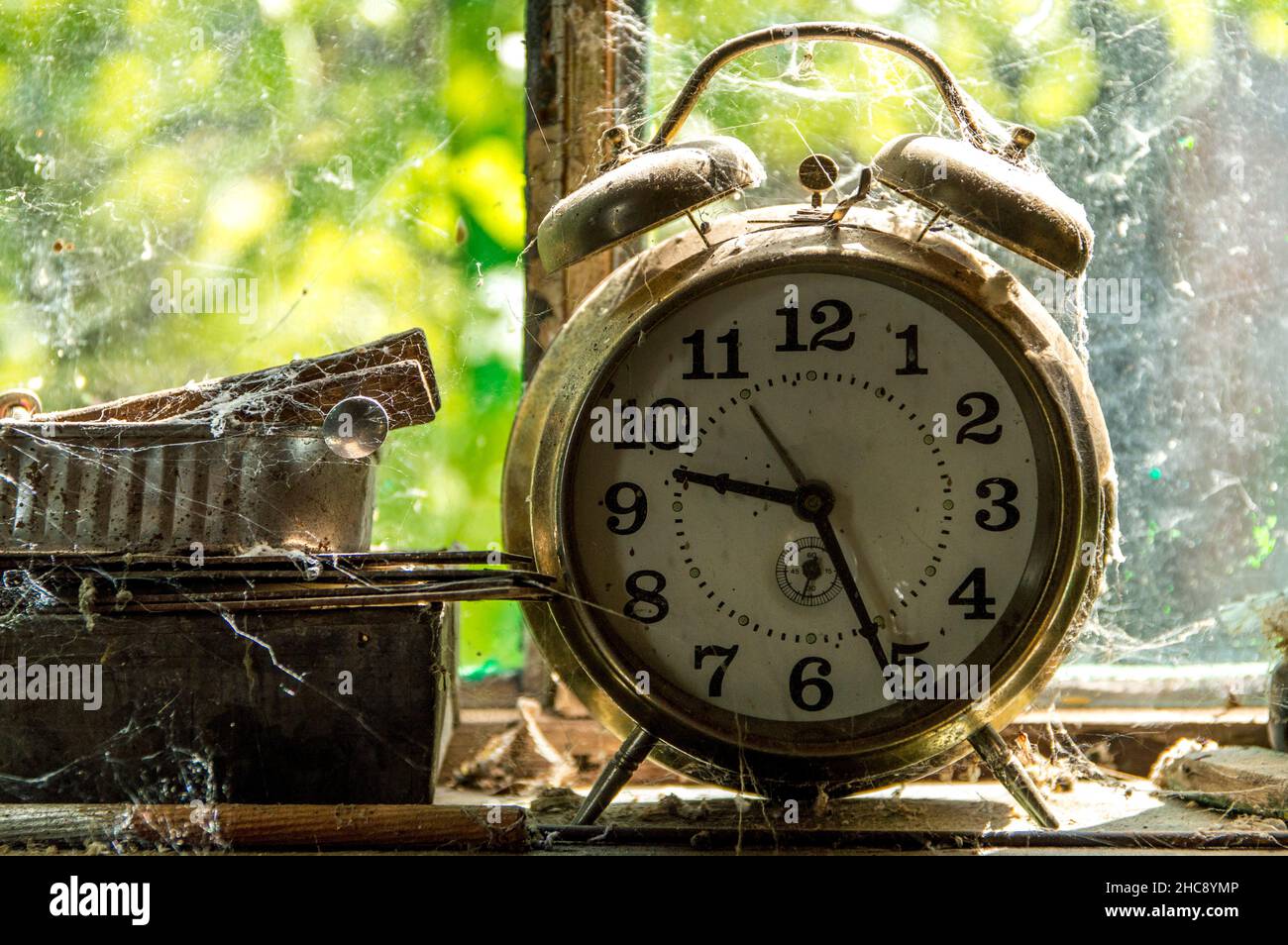 Old dusty analog clock covered with cobwebs in a window of a workshop ...