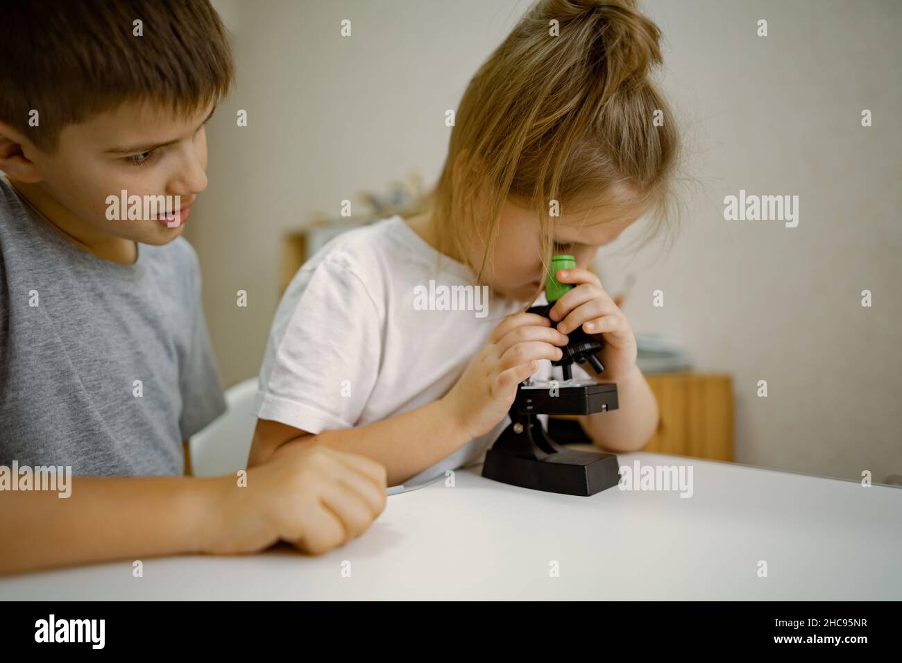 Children, girl and boy at home in the room look through microscope ...
