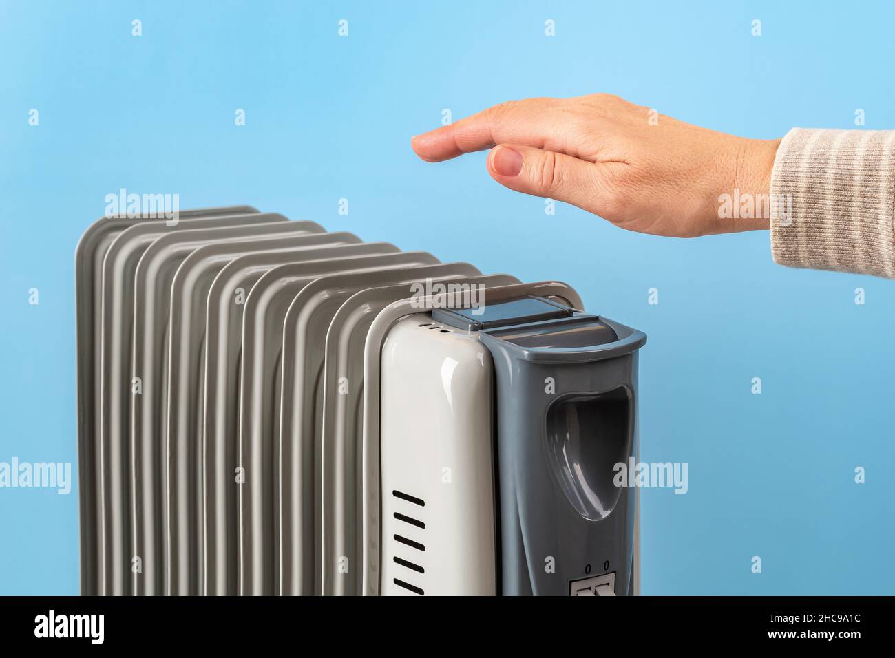 Woman hand gettin warm over hot oil filled electric heater against blue ...
