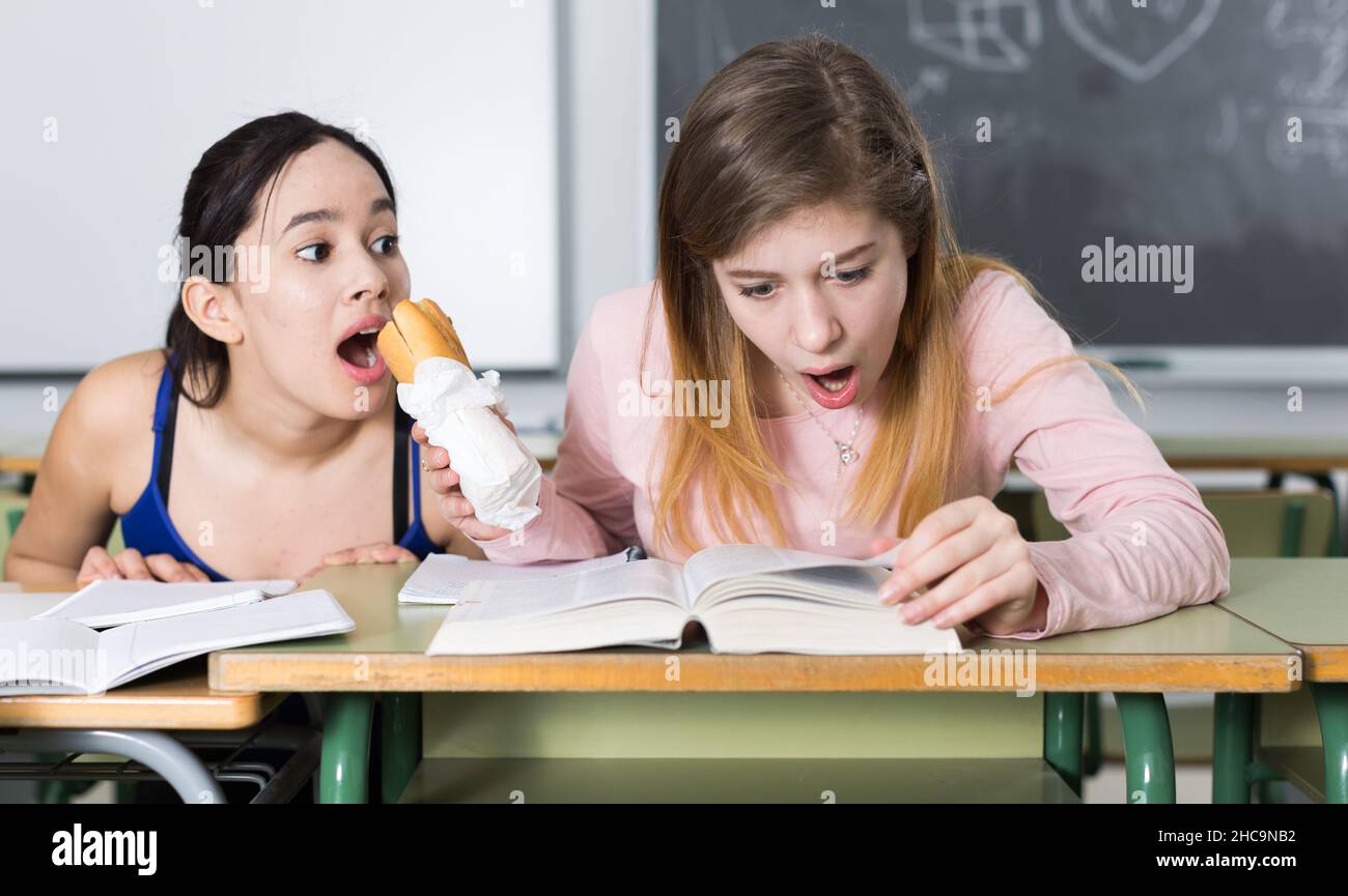 Young girls are eating lunch at the desk and reading text in the ...