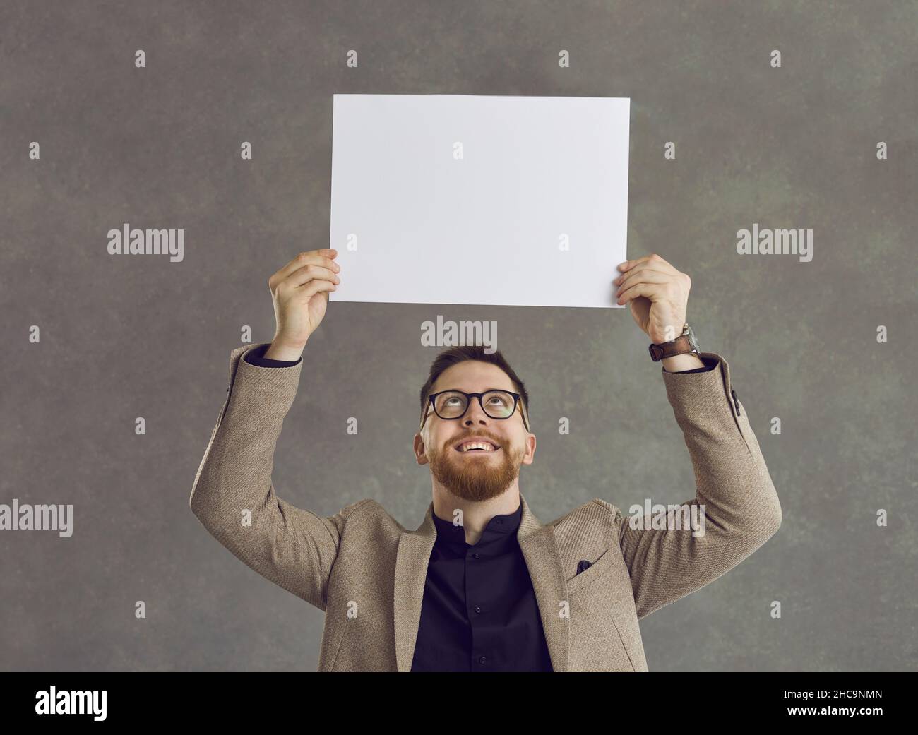 A young man with glasses and a red beard holds a white blank piece of ...