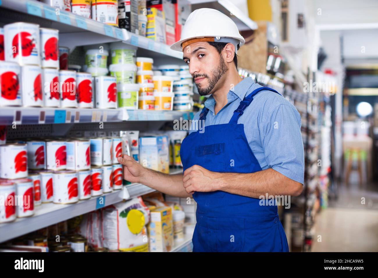 Focused workman choosing materials for renovation works in paint store ...
